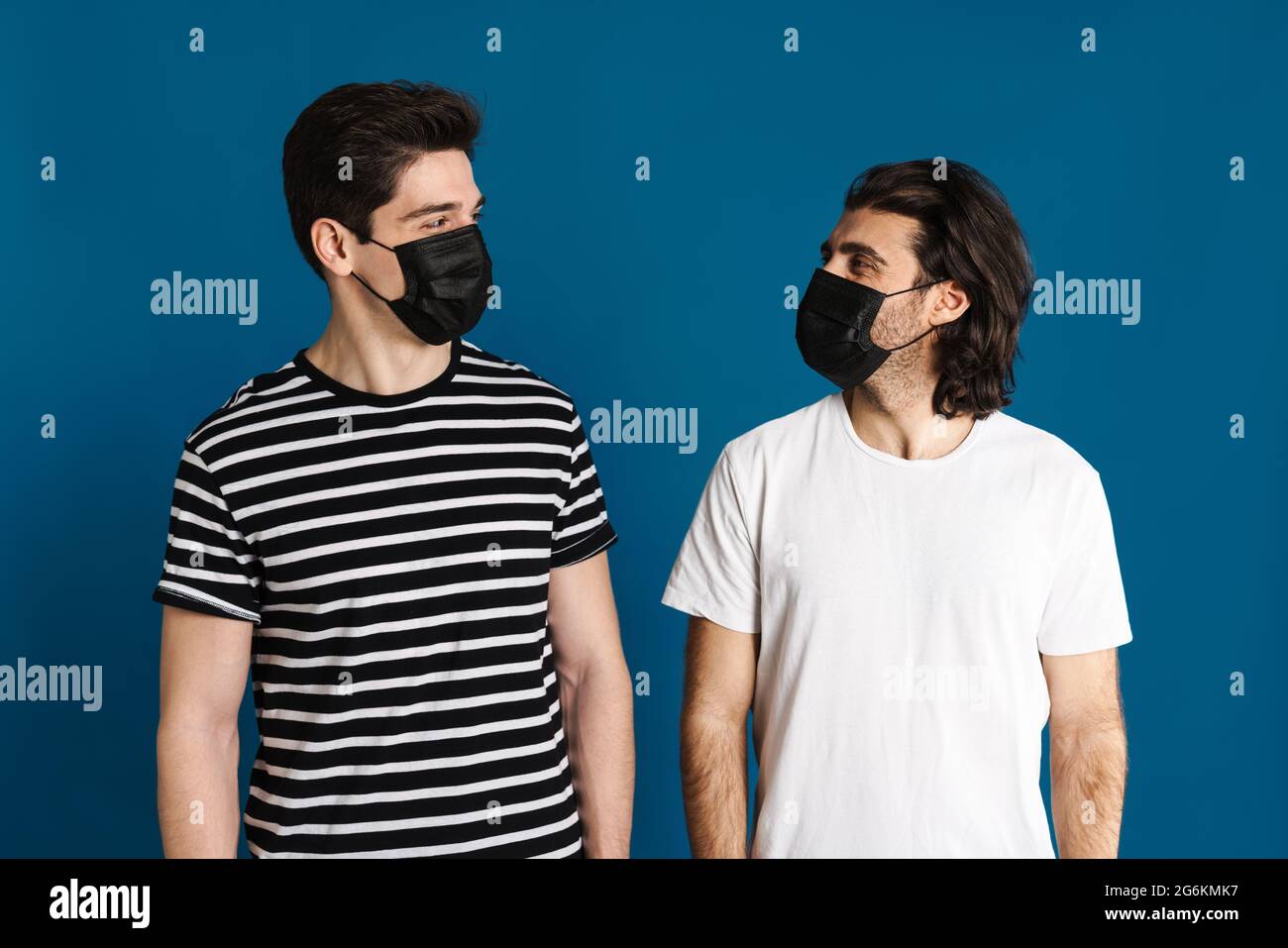 White brunette two men in face mask looking at each other isolated over ...