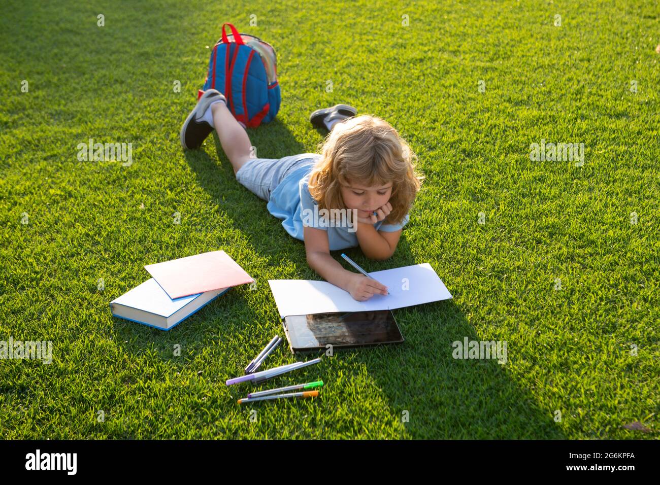 Cute boy reading book on green grass writing notes in copybook ...