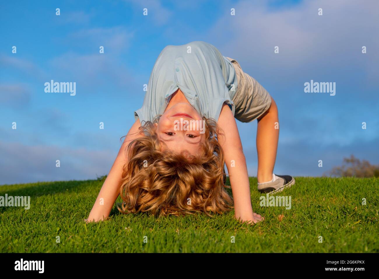 Happy child standing upside down on green grass. Laughing kid boy ...