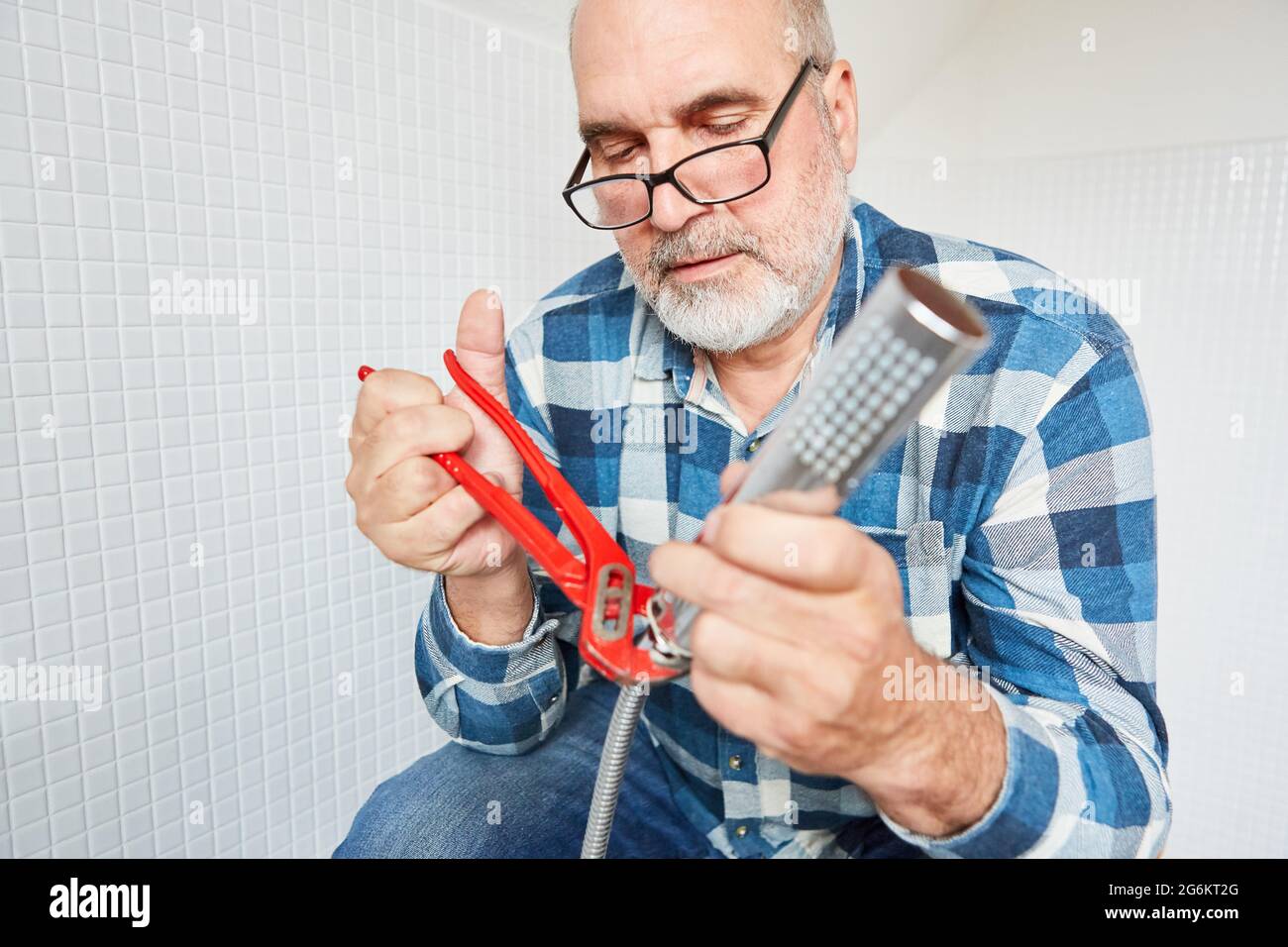 Plumber handyman with pipe wrench repairing the shower head and hose in ...