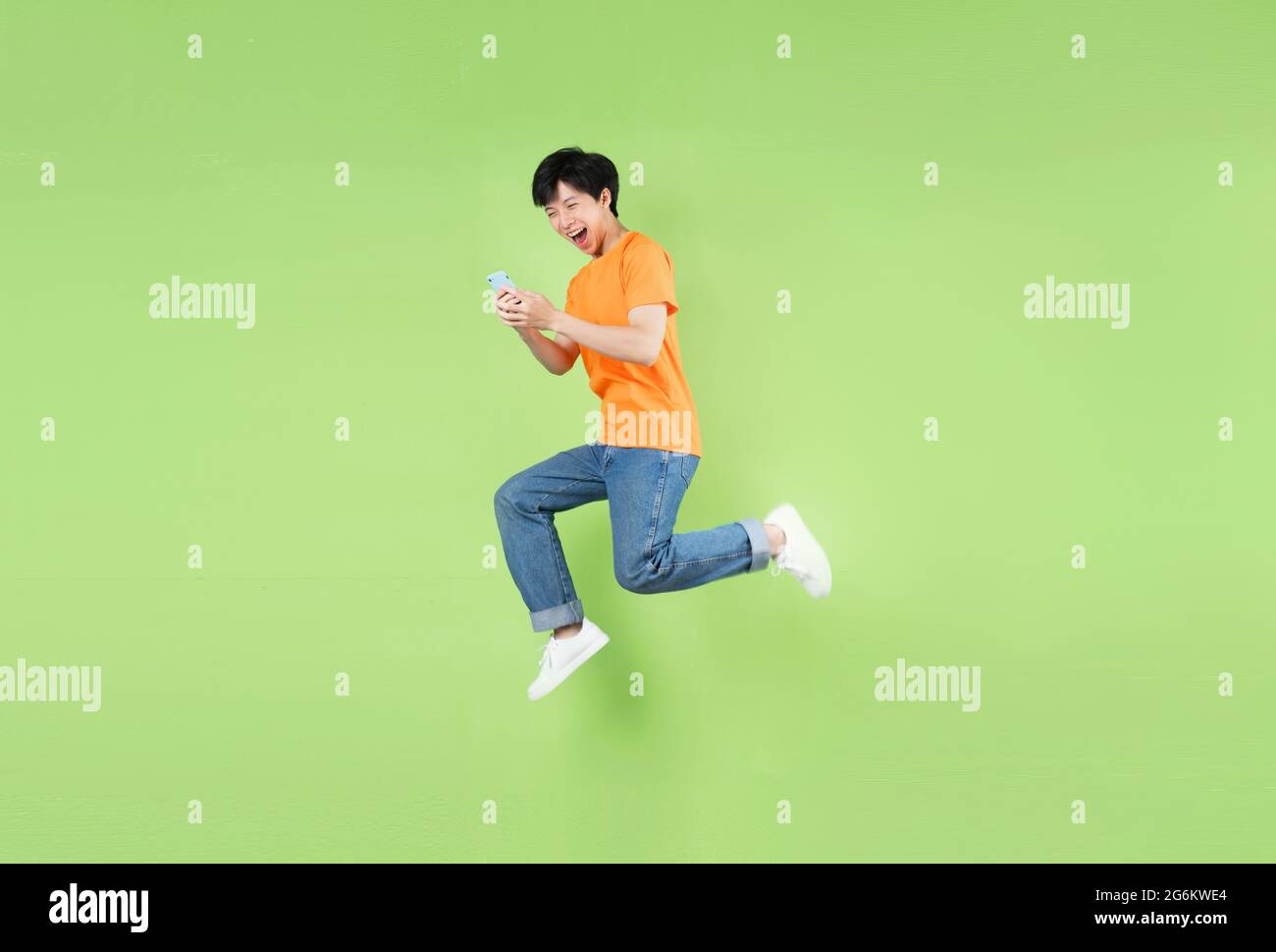 Asian man jumping and holding smartphone , isolated on green Stock ...