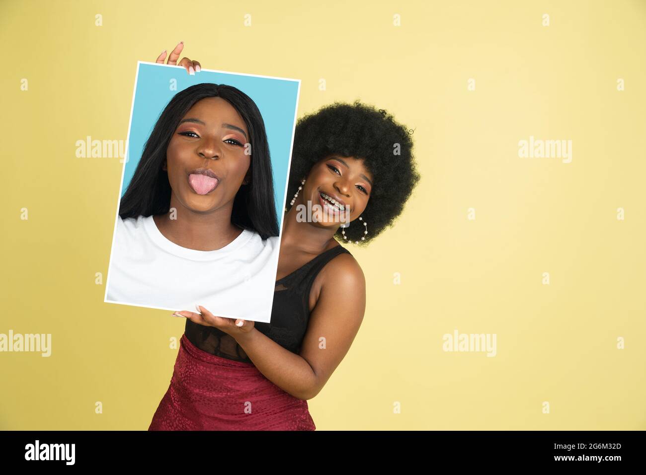 Young African girl holding her portraits isolated over yellow studio ...