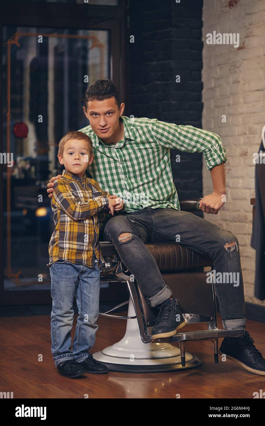 Young handsome father and his little stylish son at barbershop waiting ...