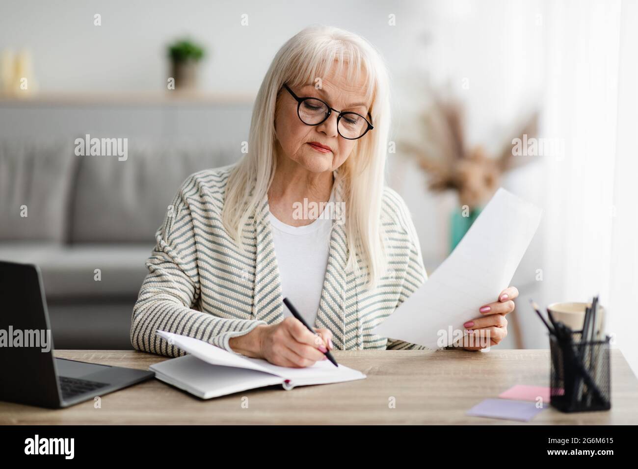 Focused mature woman writing and holding document at home Stock Photo ...