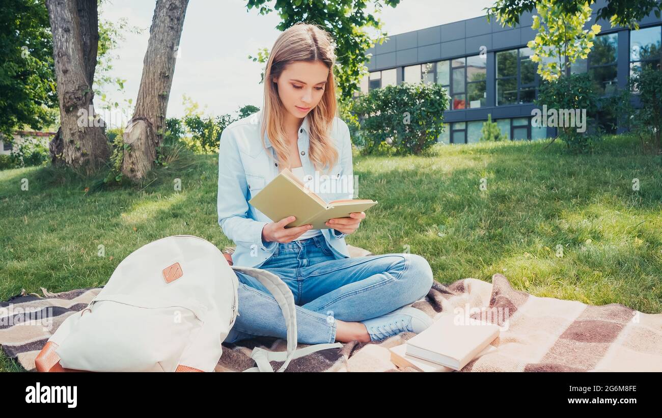 young woman with crossed legs sitting on blanket and reading book Stock ...