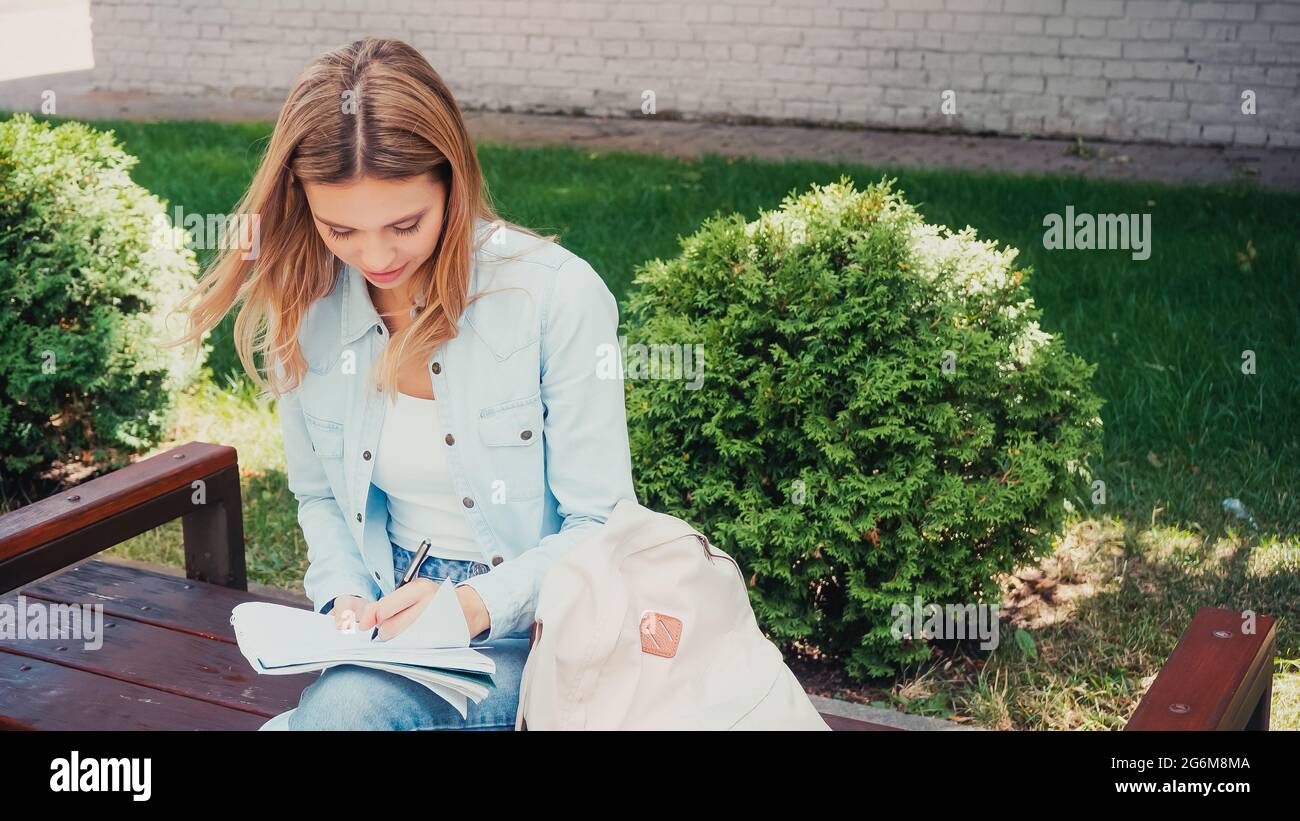 Student writing in notebook while sitting on bench outside Stock Photo ...