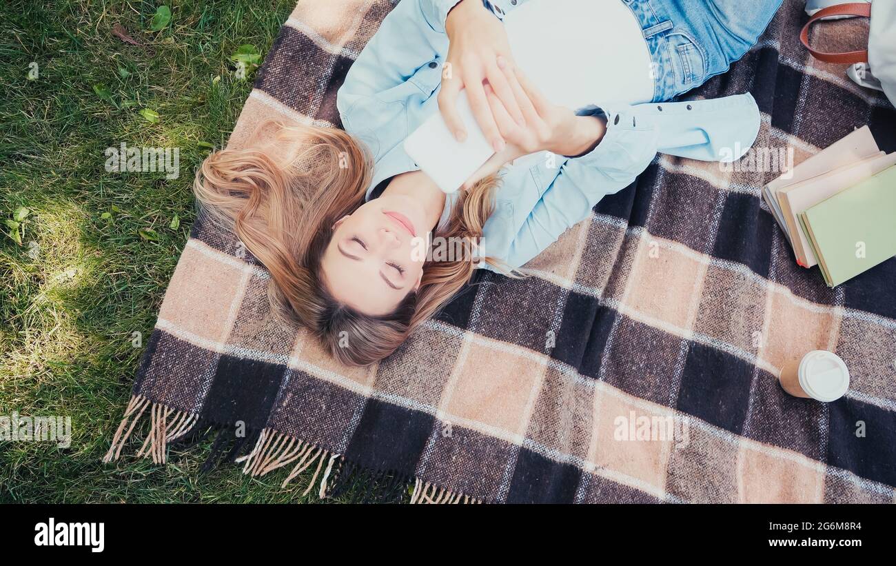 Top view of happy student using smartphone near coffee to go and books ...
