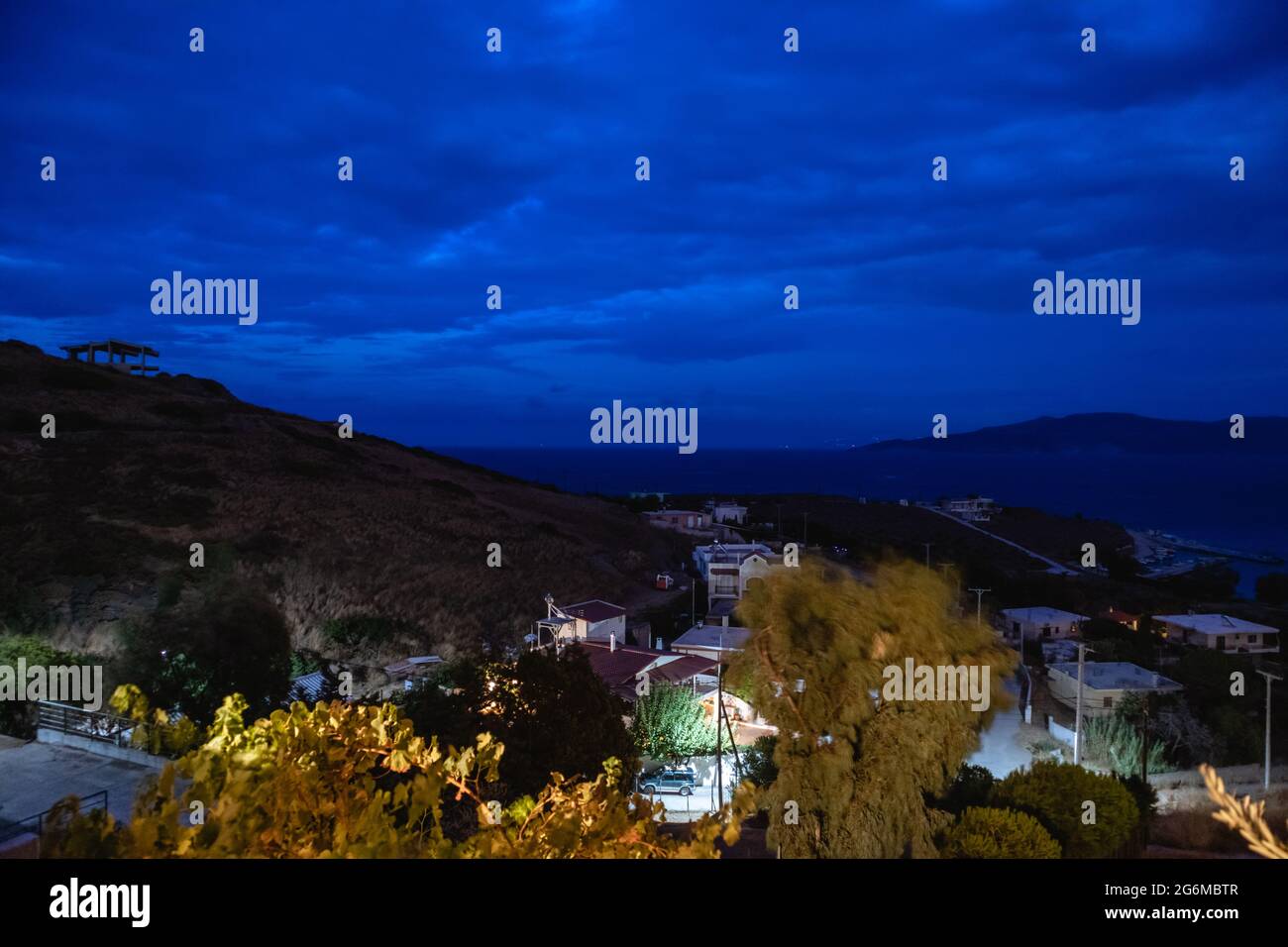 Night summer sea coast in greek village with olive trees waving in wind ...