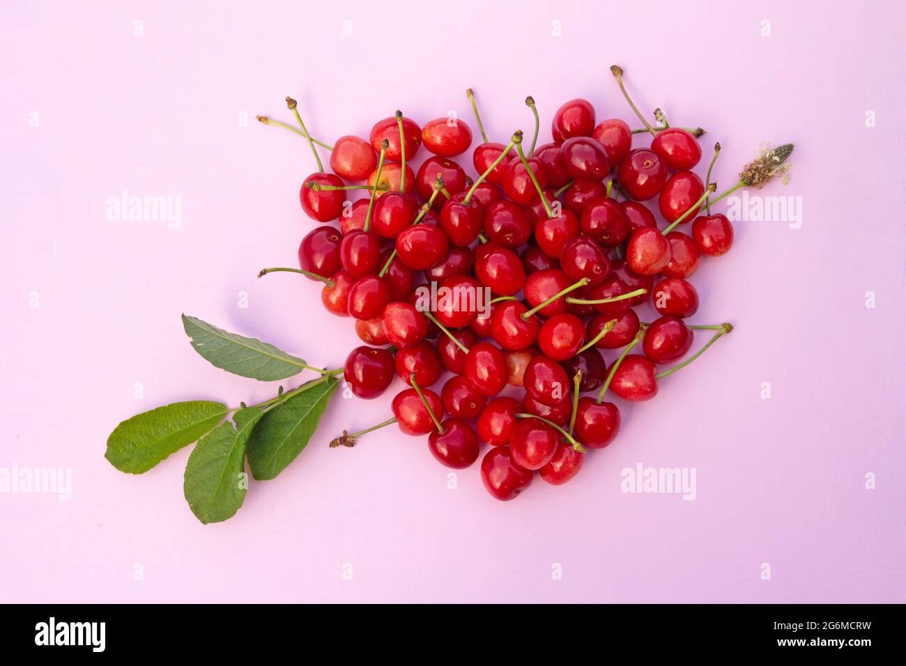 Red sweet cherries in heart shaped layout with arrow of green branch on ...