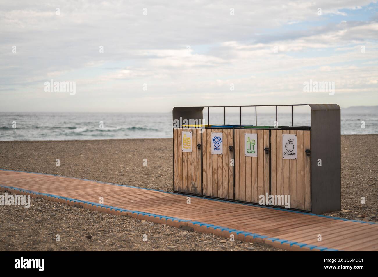 recycling containers in front of a wooden path on the beach with the ...