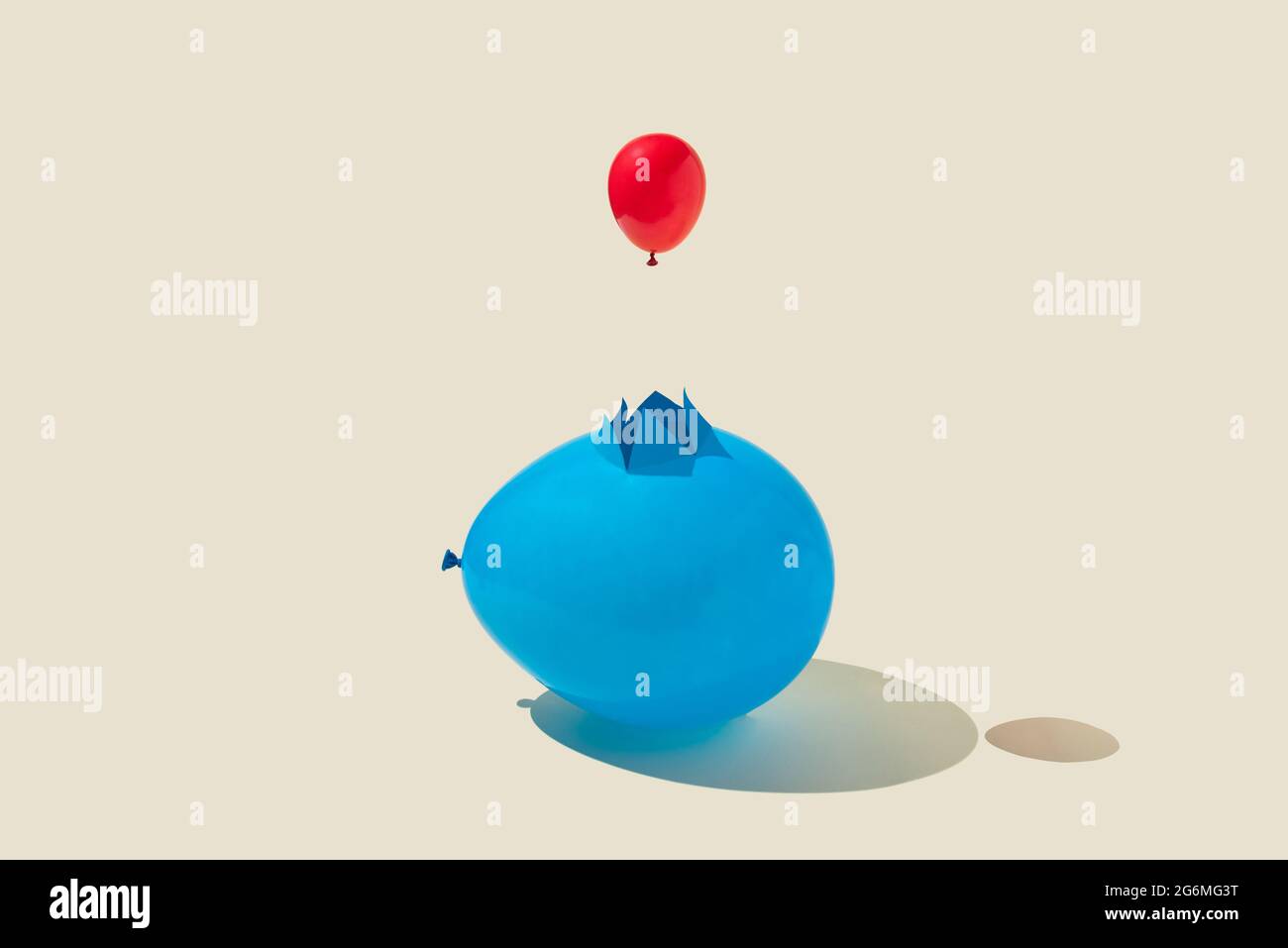 Small red party balloon comes out of a cracked large blue one on yellow ...