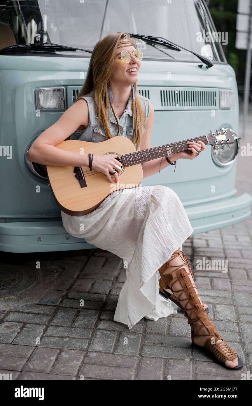 Dreamy woman sits by the camper. A hippie girl holding a guitar and ...