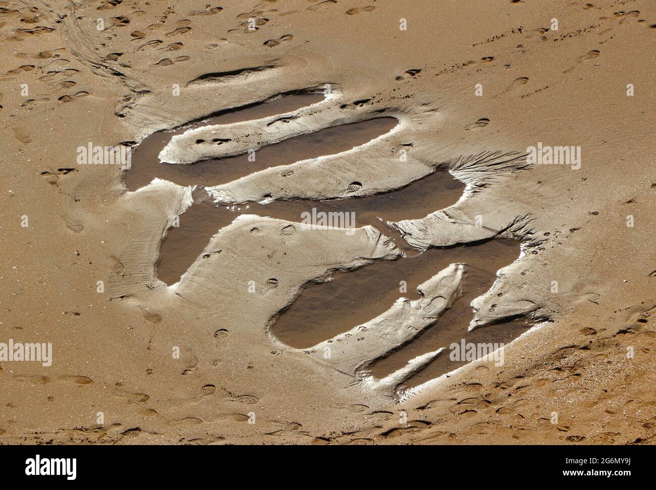 Strange shaped puddles on a beach with footprints in the sand Stock ...