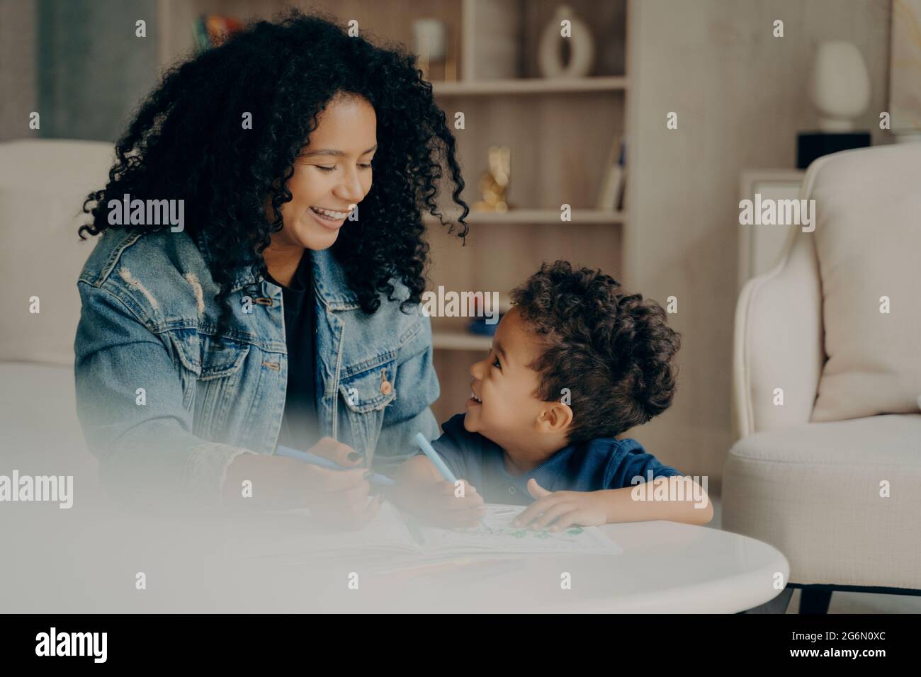 Loving happy woman with long curly hair playing with little son at home ...