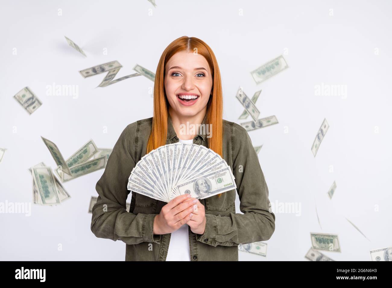 Portrait of attractive cheerful red haired girl holding cash salary ...