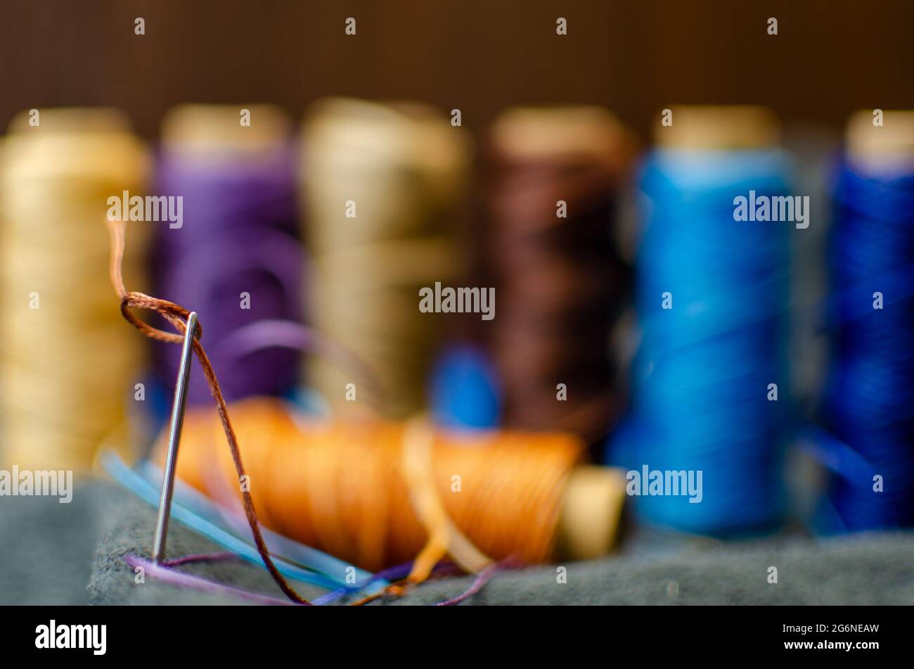 brown thread inserted into the eye of the needle against the background ...