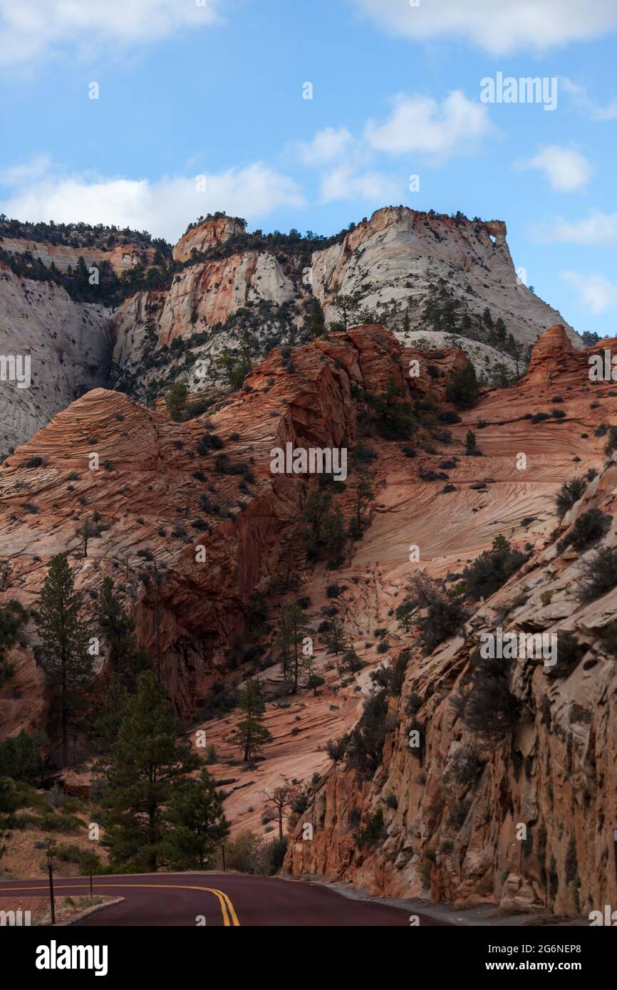 A red asphalt road at the base of towering sediment to stone mountains ...
