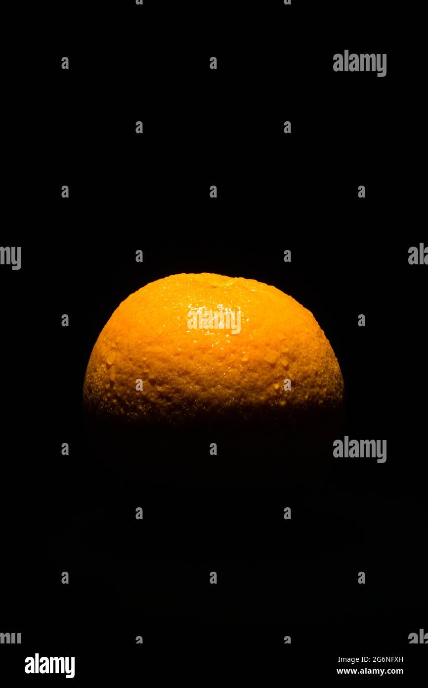 Dark low key image of a fresh and ripe orange fruit lit from above only ...