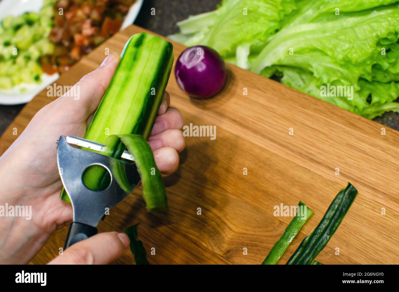 The process of peeling a cucumber close up. A woman in an apron peels a ...