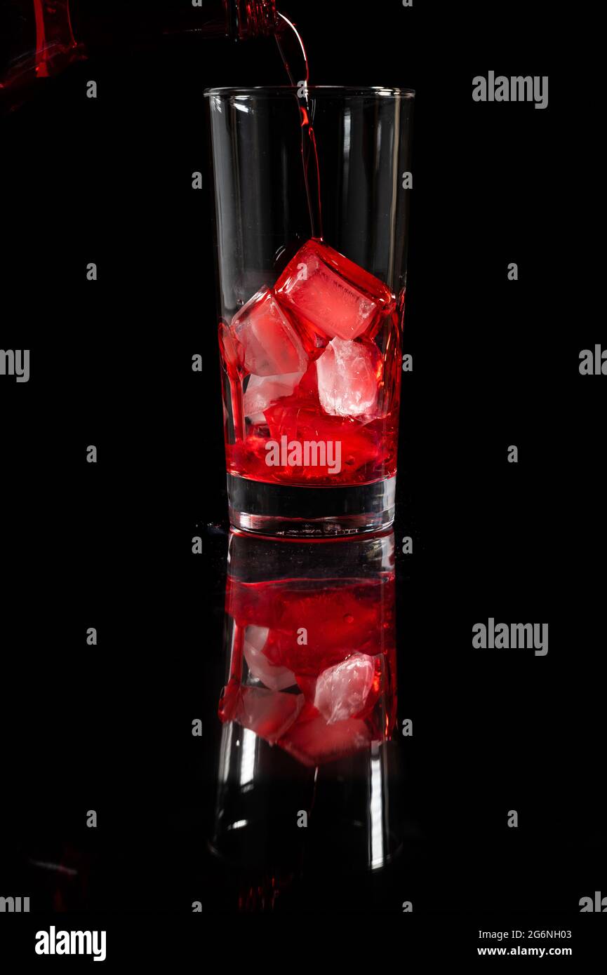 Pouring red juice on the top of the ice into the glass against complete ...