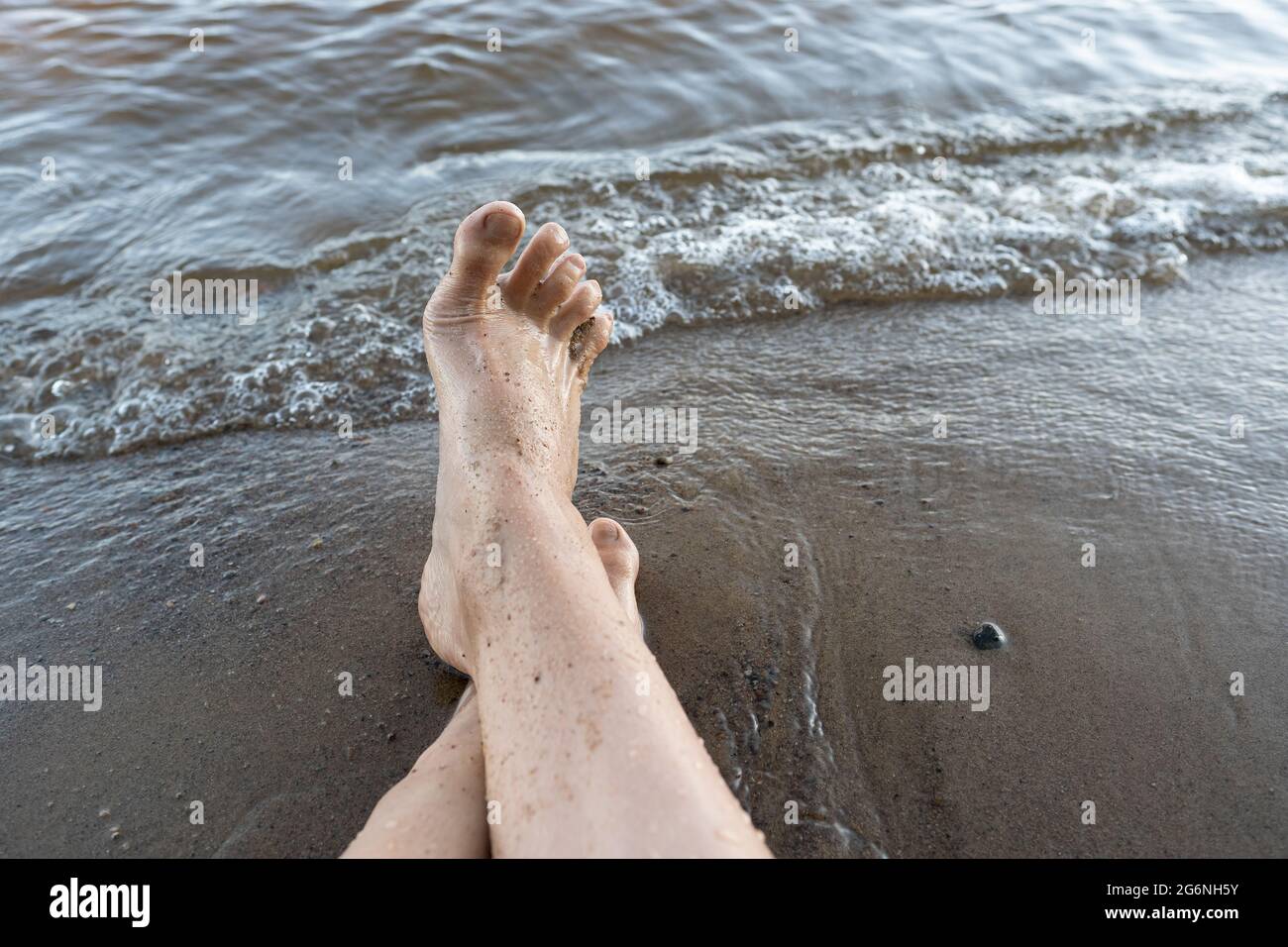 Wet female feet on a sandy beach near the water. Woman is resting while ...