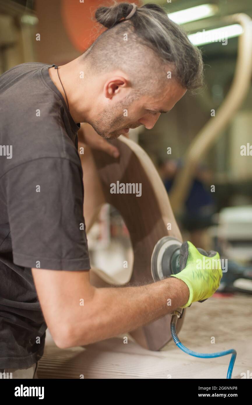 Craftsman is using an electric sander, to smoothen the wood texture ...