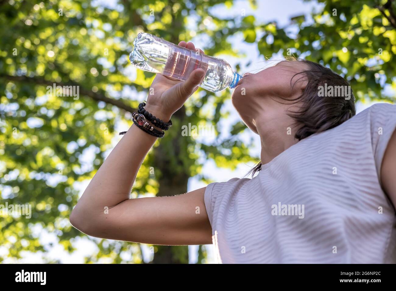 Woman drinks cool drinking water from a plastic bottle on a hot summer ...