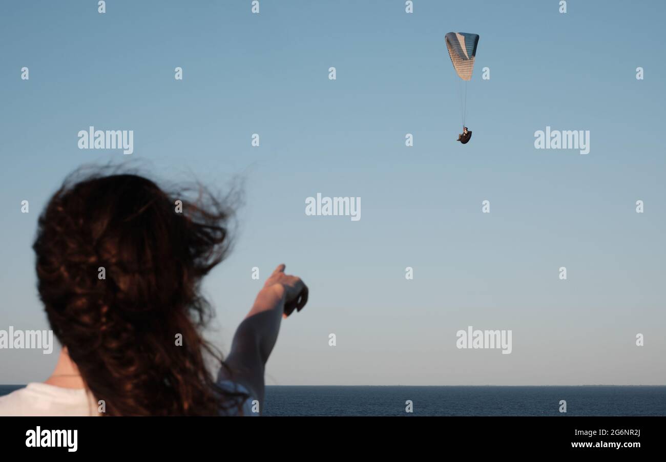 Woman points to the flying paraglider. Paraglider soars in the sky ...