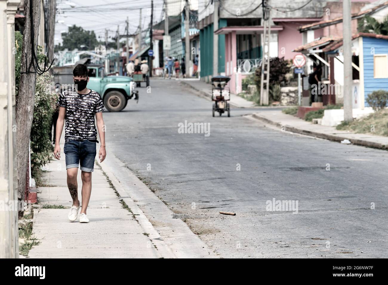 Young Latin male walking along the sidewalk wearing a black surgical ...