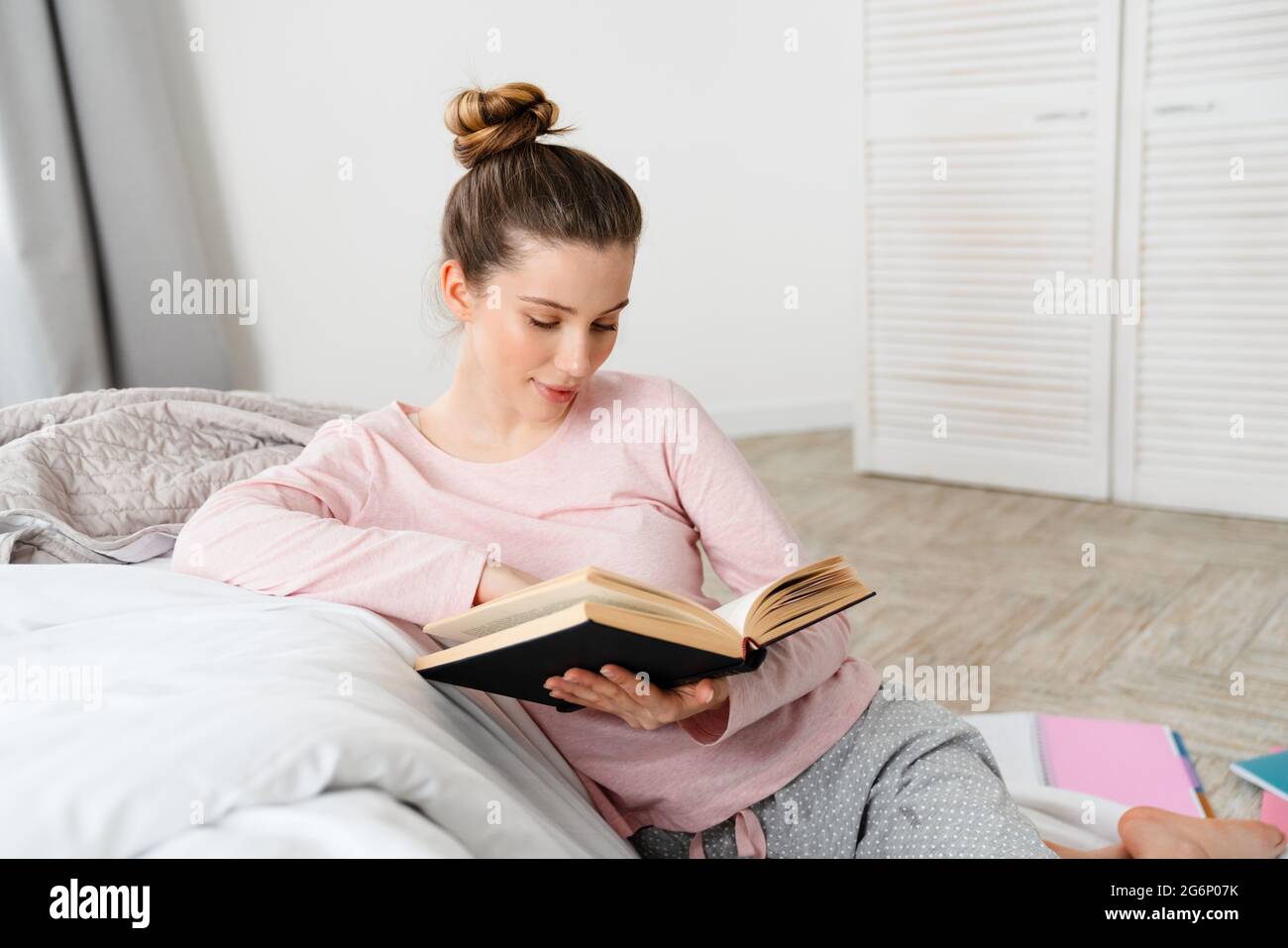 Young smiling white woman reading book studying sitting on a floor of ...