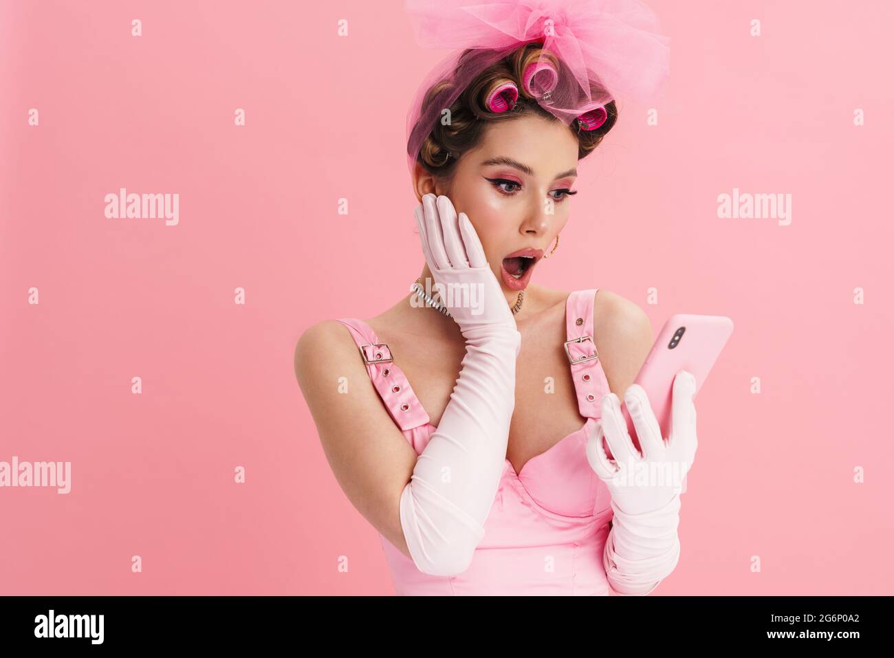 Surprised woman with curlers exclaiming while using mobile phone ...