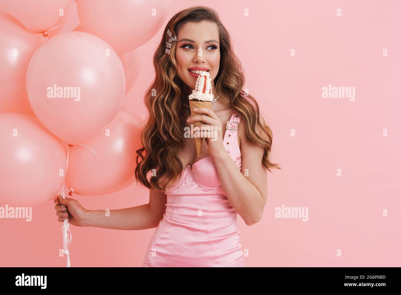 Young smiling woman eating ice cream while posing with balloons ...