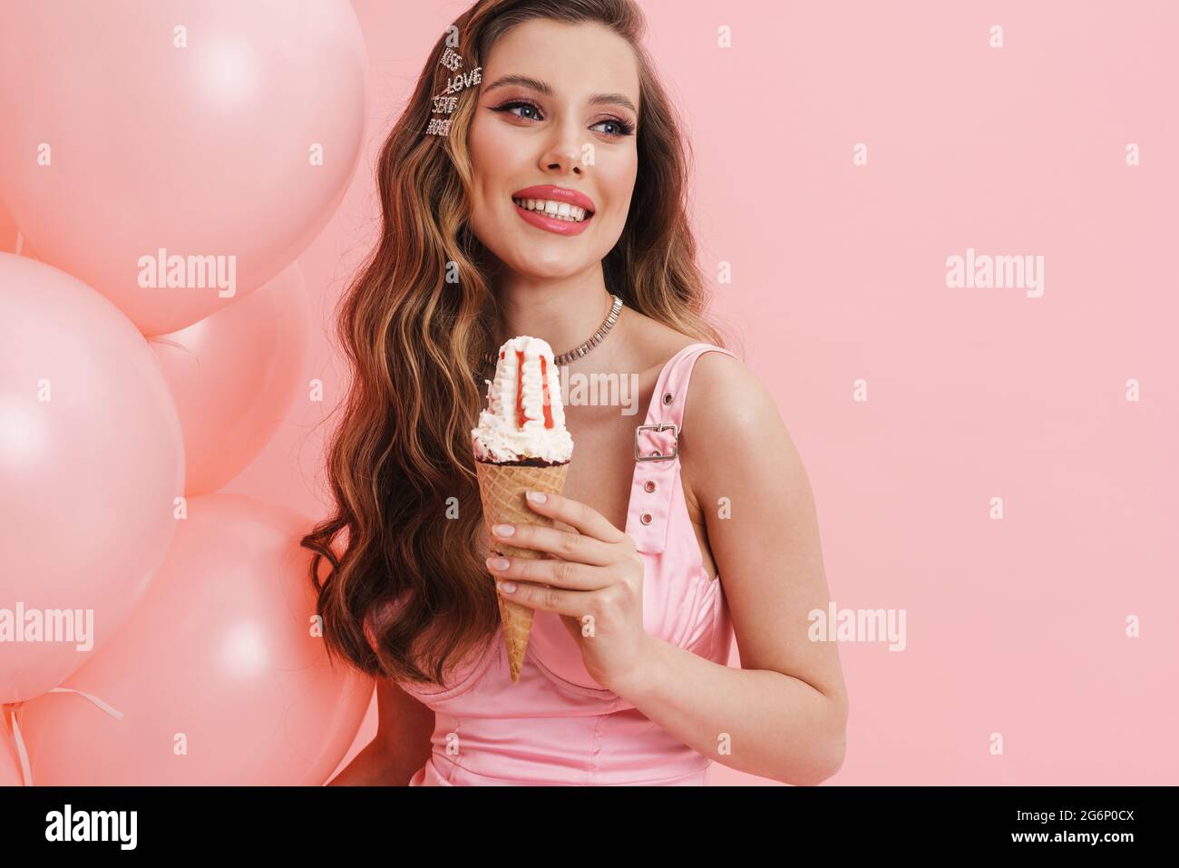 Young smiling woman eating ice cream while posing with balloons ...