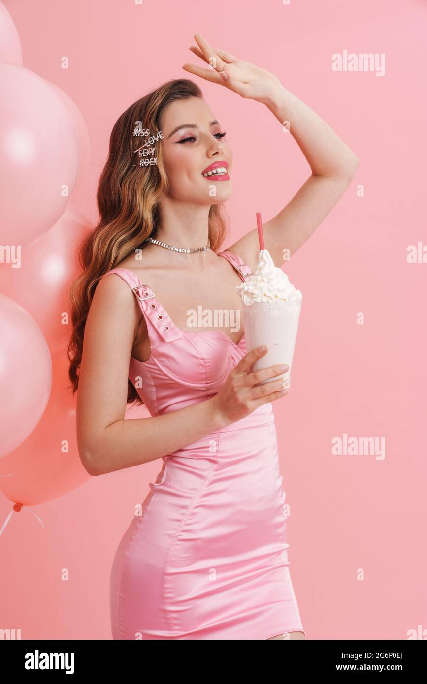 Young smiling woman wearing dress posing with balloons and milkshake ...
