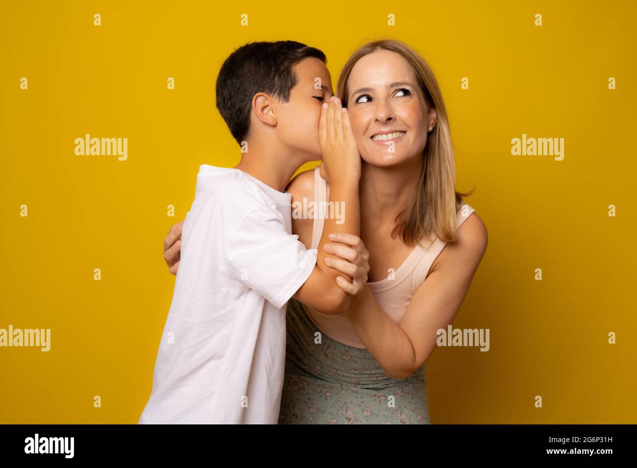Boy telling his mother a family secret isolated over yellow background ...