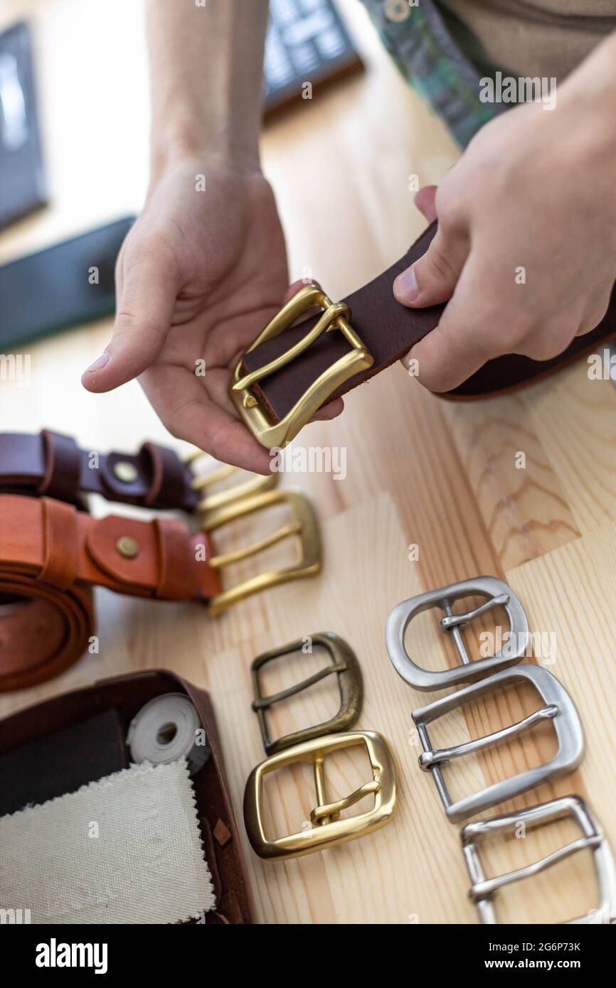 Closeup hands of professional tanner choosing belt buckle on wooden ...