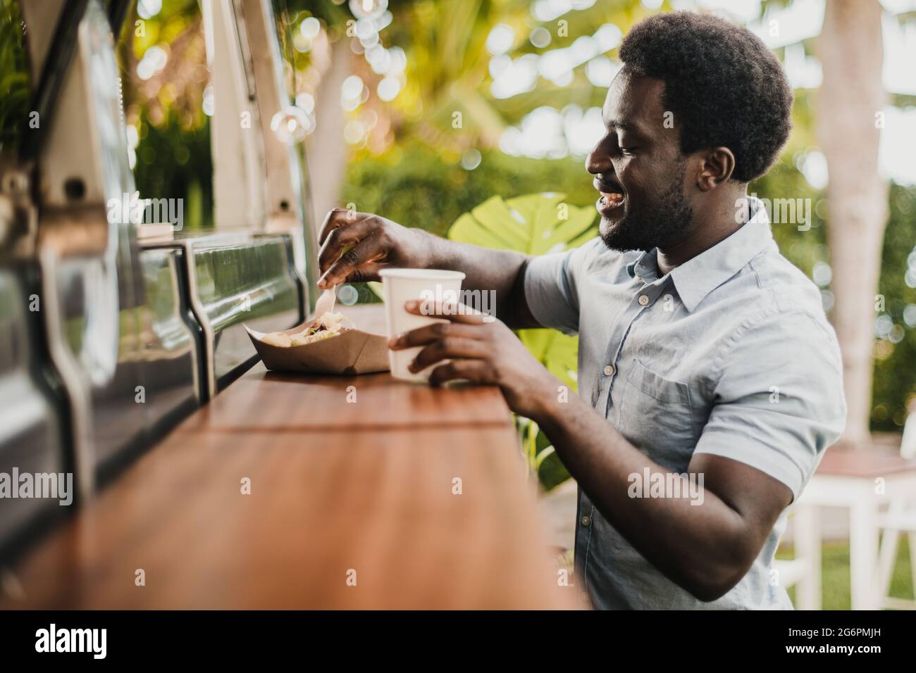 Young african man eating in food truck counter outdoor in city park ...