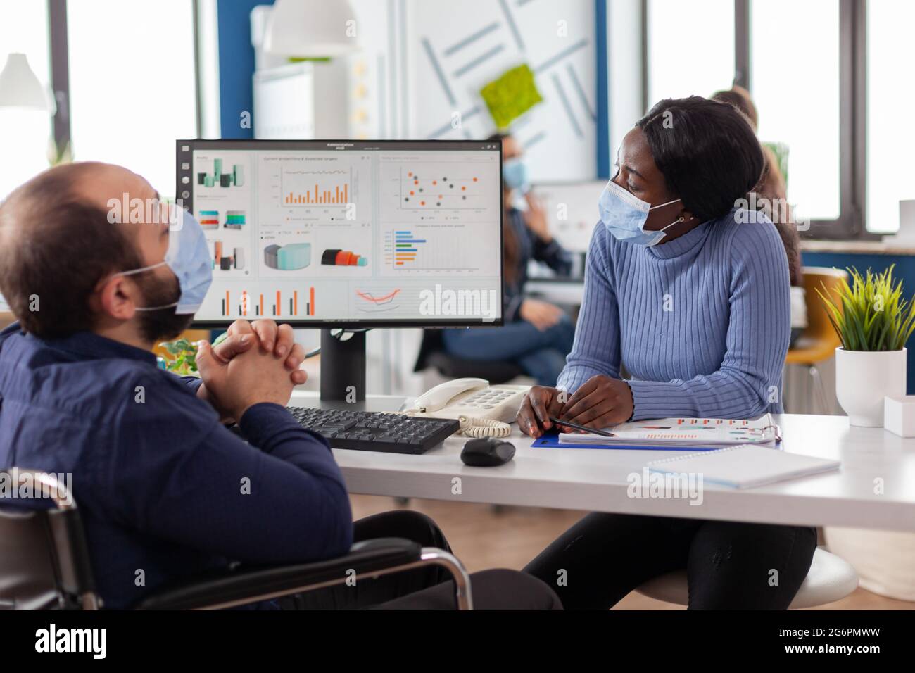 Diverse colleagues with masks respecting social distance working with ...