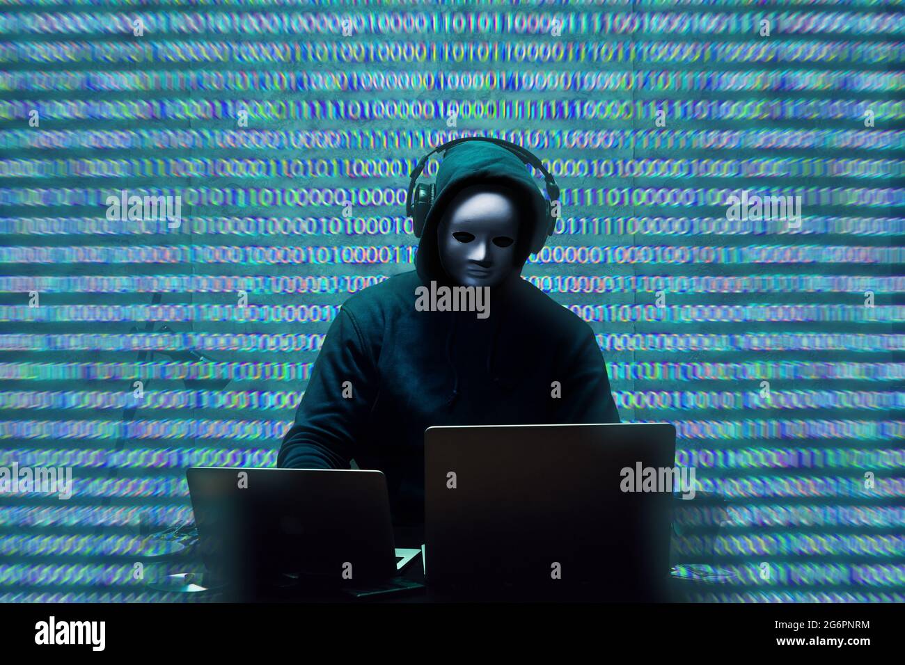 Anonymous hacker wearing face mask working on computer in dark room ...