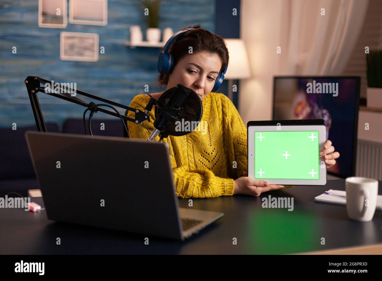Influencer holding tablet with green screen and speaking into ...