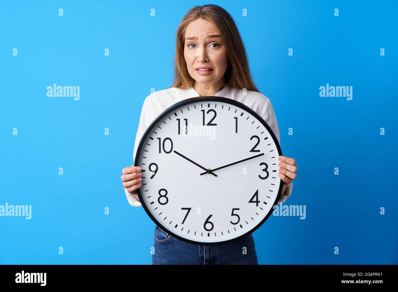 Attractive young woman holding big wall clock against blue background ...