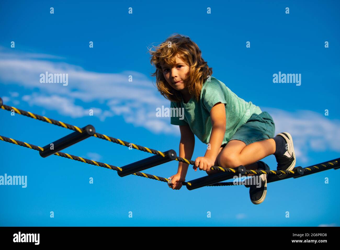Kid climbing the net. Cute boy climbs up the ladder on the playground ...