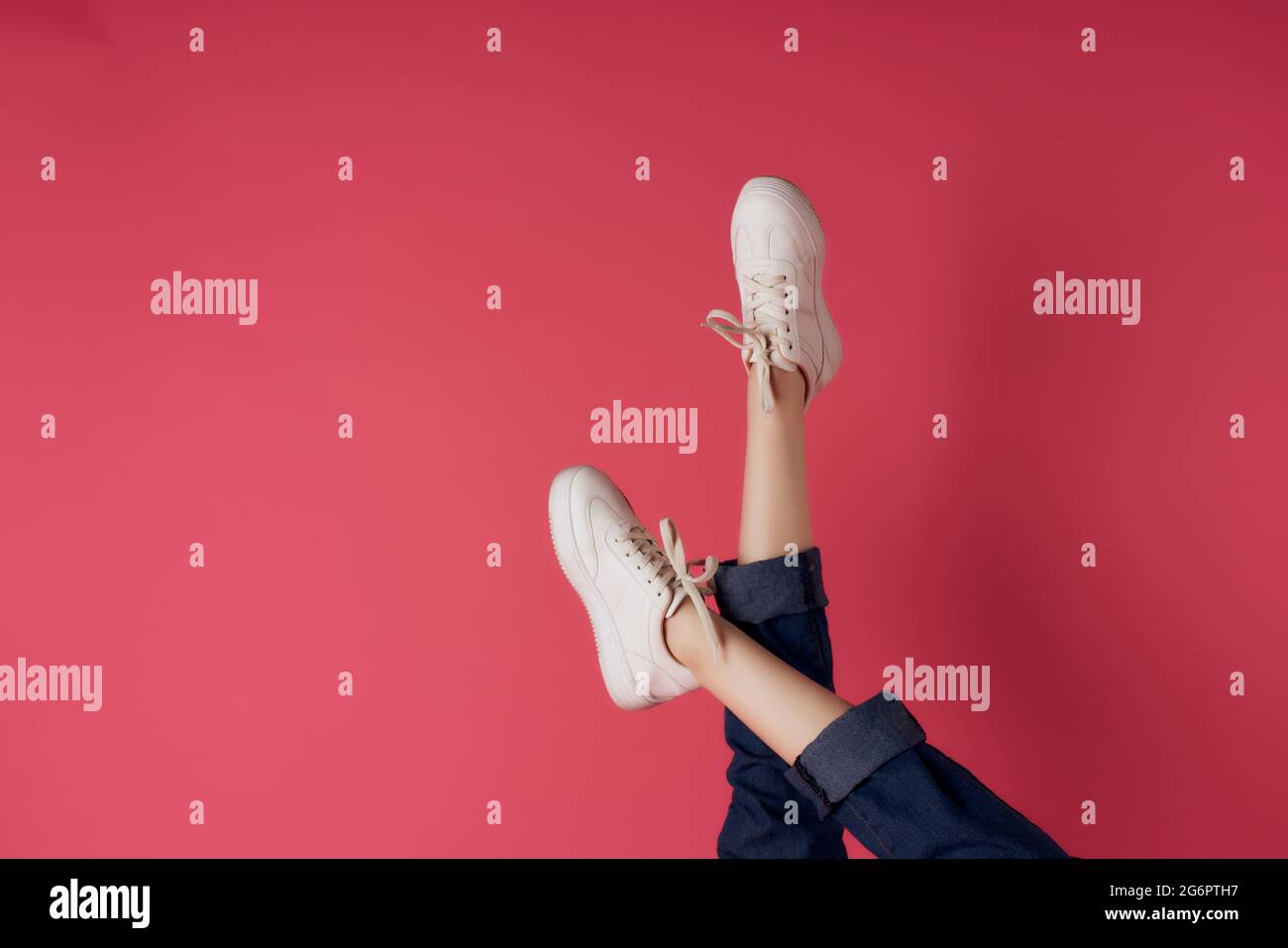 inverted female legs in white sneakers pink background cropped view ...