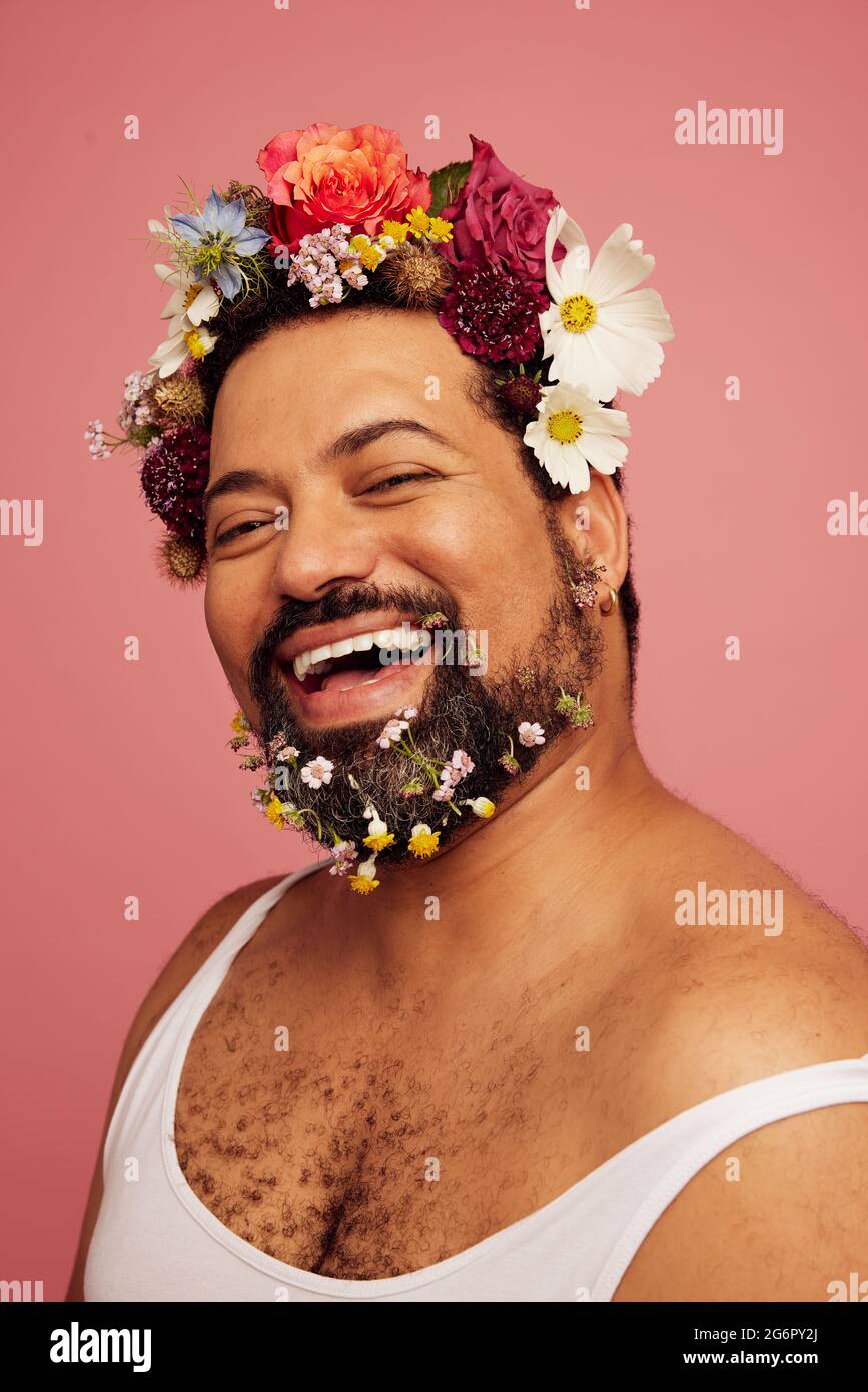 Cheerful male with flowers in hair and beard. Gender fluid man looking ...