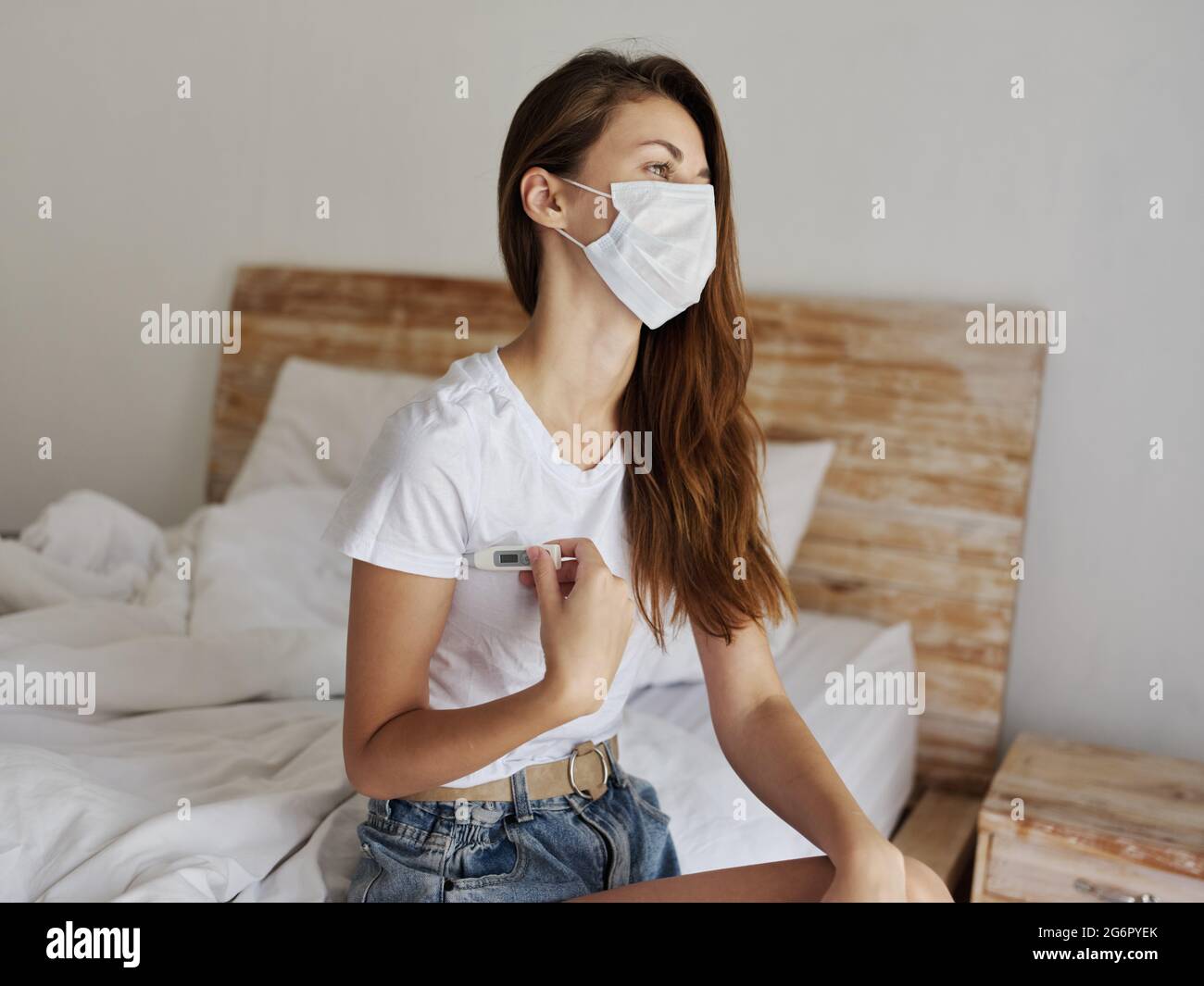 woman with thermometer under her arm wearing medical mask checking ...