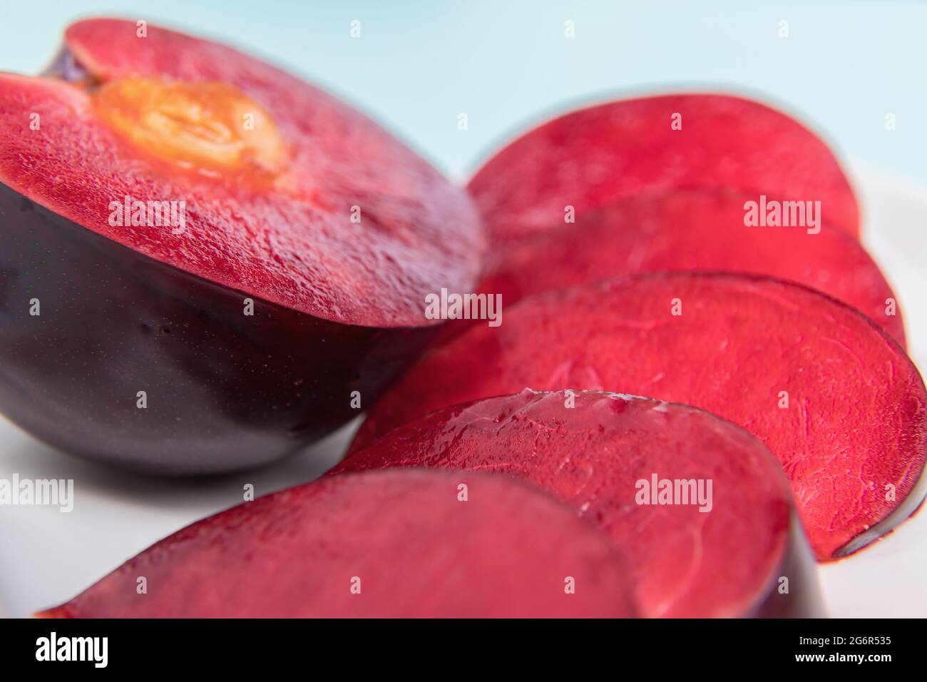 On a white saucer, a large plum, cut in half, with slices next to it ...