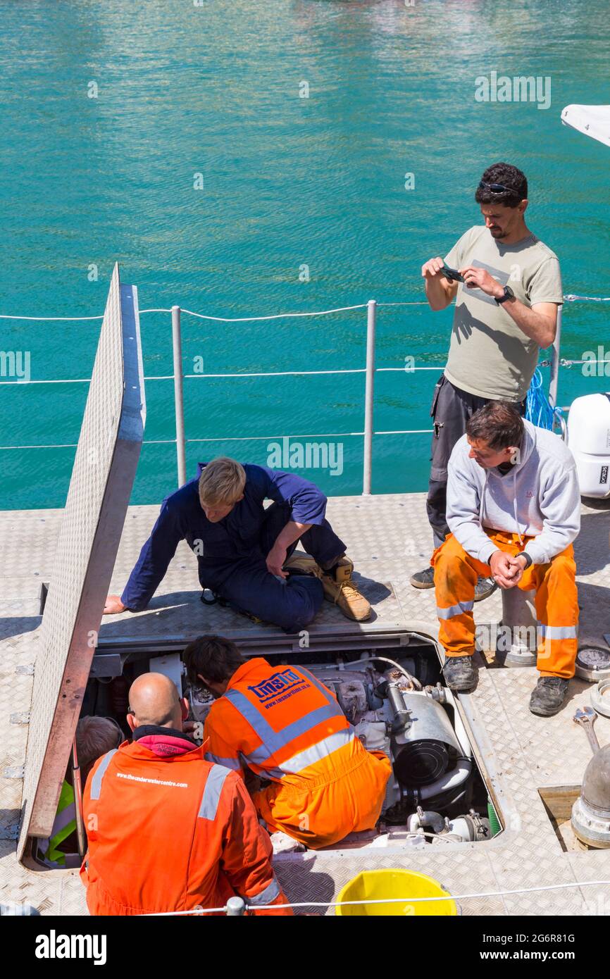 Men working on engine motor on boat at Padstow, Cornwall UK in June ...