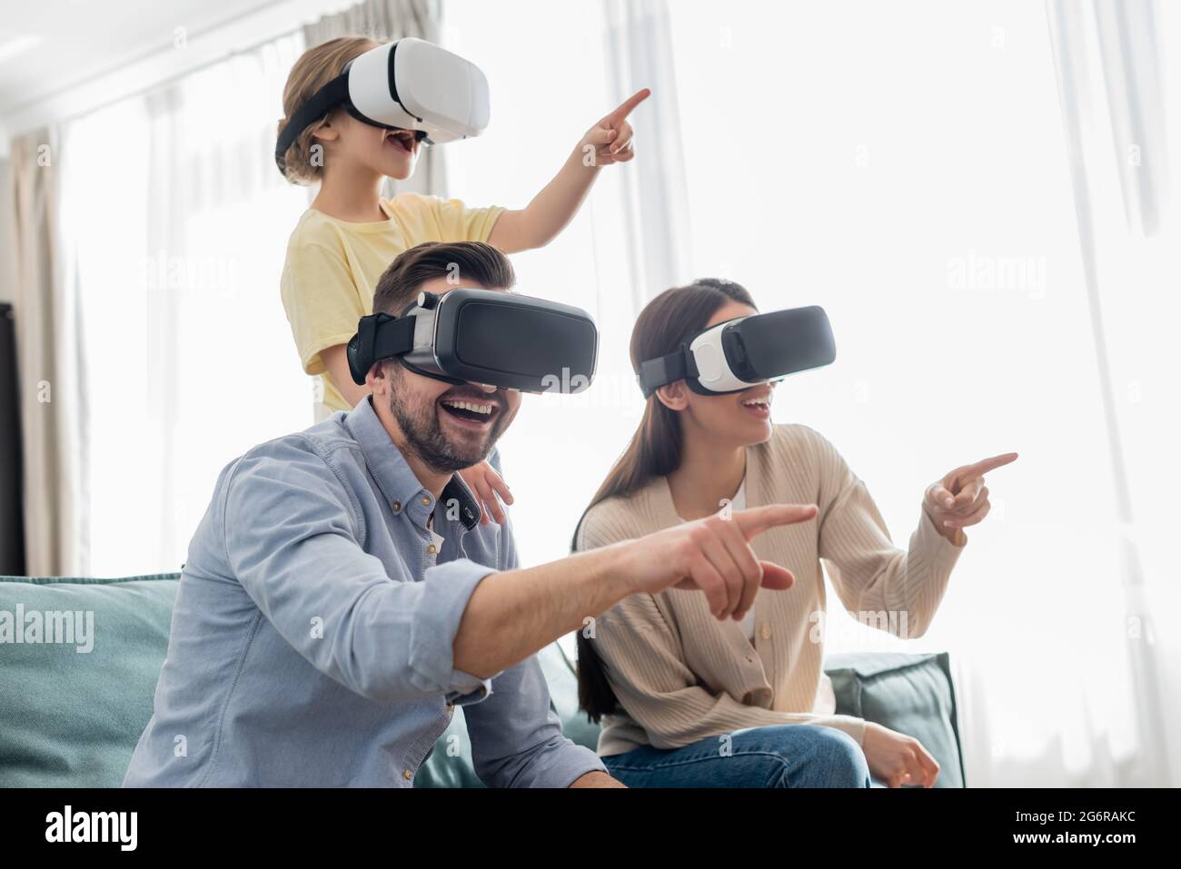 cheerful family gaming in vr headsets and pointing with fingers at home ...