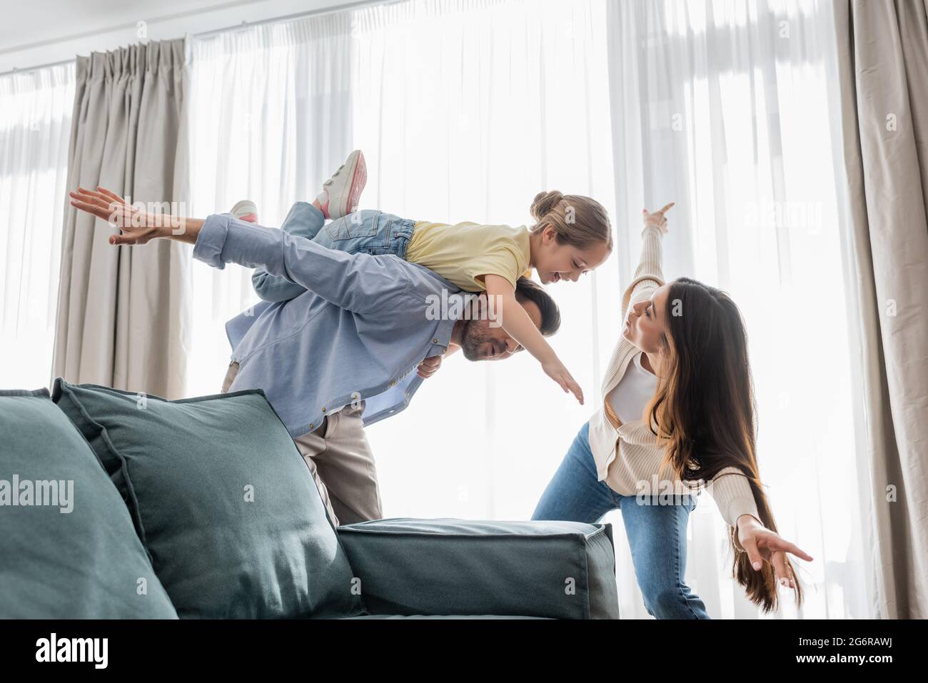 joyful girl piggybacking on back of father and imitating plane with mom ...