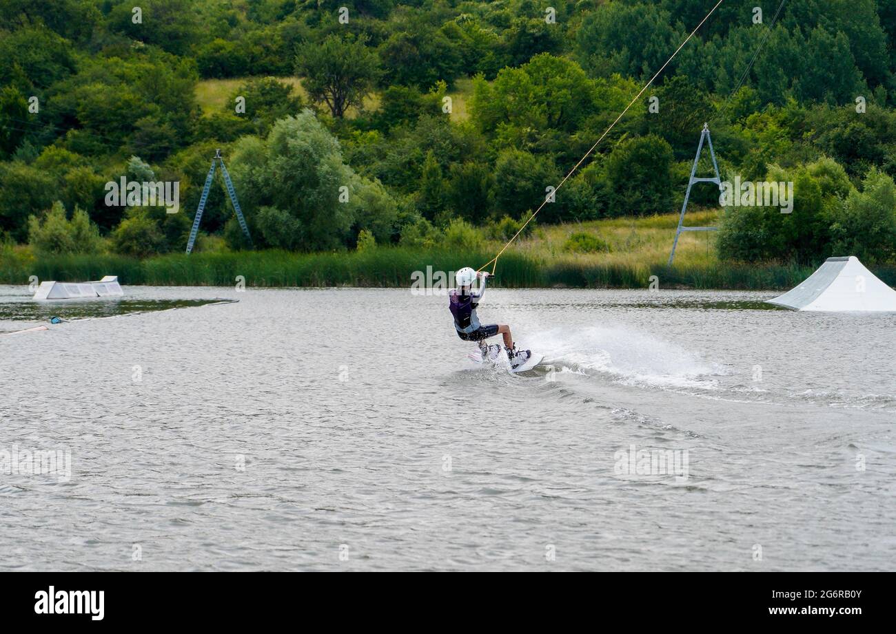 Athletic Woman wakeboarding on a lake with green hills during sunny day ...